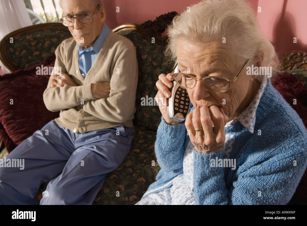 Senior woman talks on cordless phone while grumpy senior man watches ...