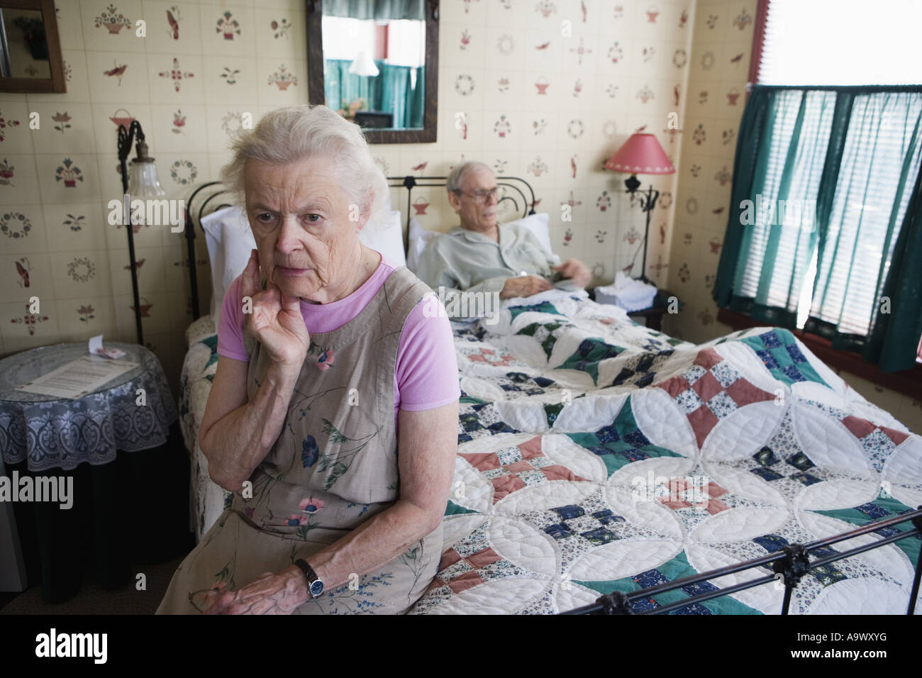 Worried senior woman sitting on bed with bedridden senior man Stock ...