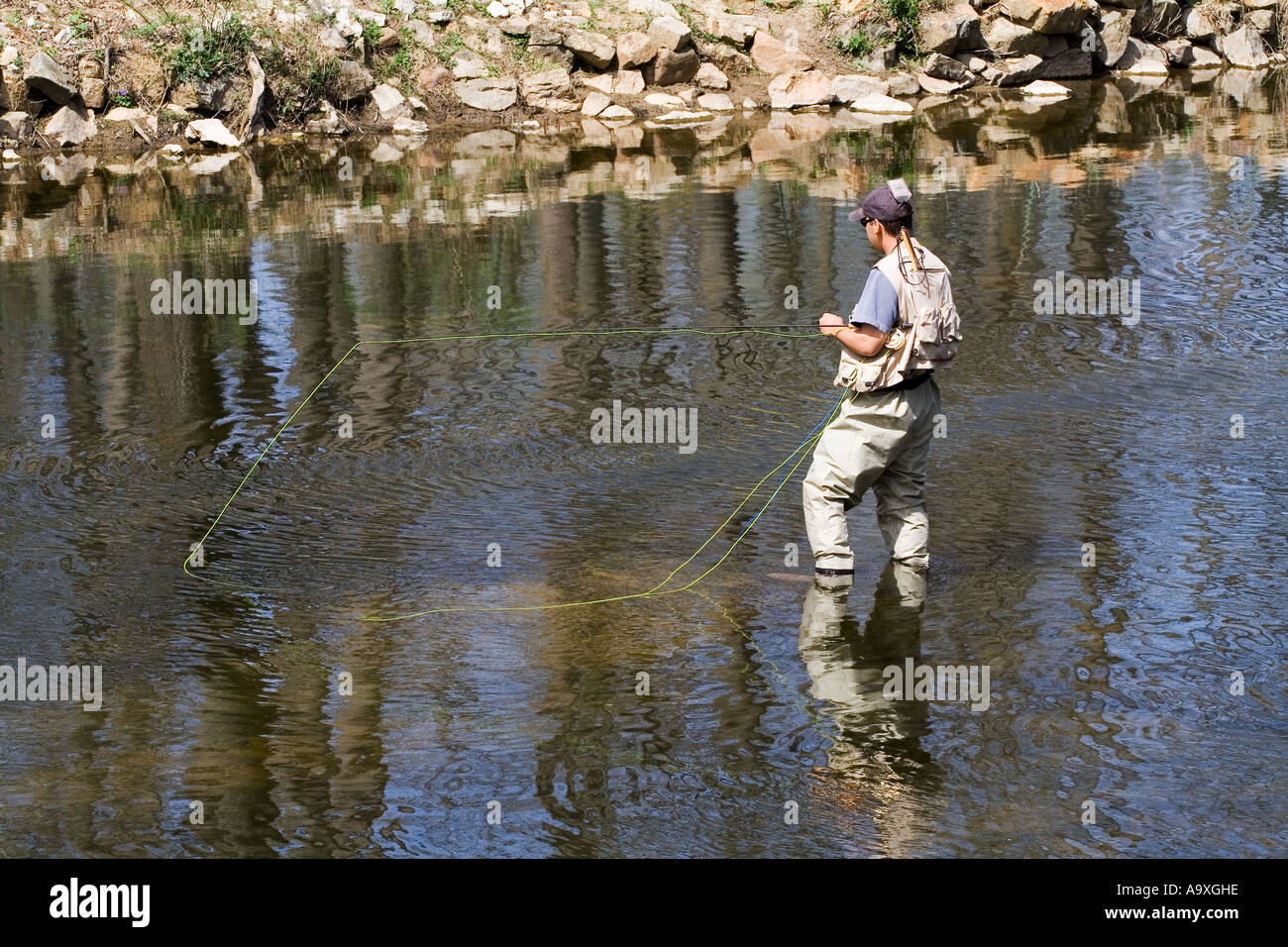 A fly fisherman taking a moment to check his fly Stock Photo - Alamy