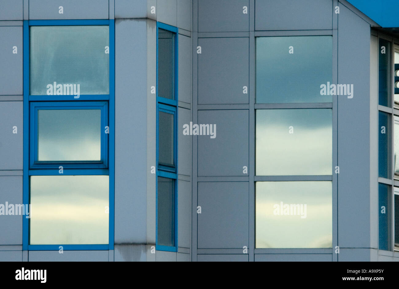 Grey wall, with blue windows reflecting grey sky Stock Photo - Alamy