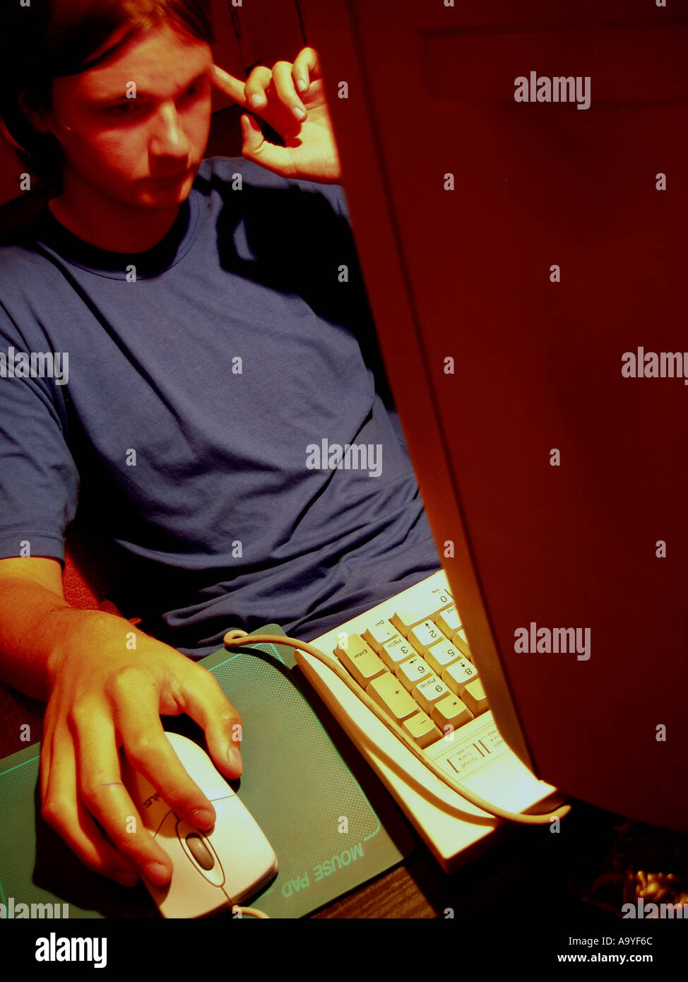 Teenager using computer with hand on the computer mouse looking into ...