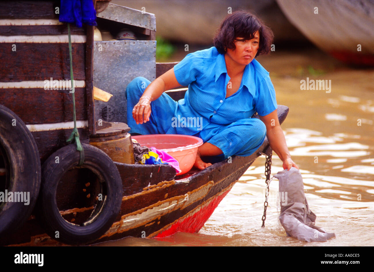 A female washing clothes from a house boat in a dirty river of Mekong ...
