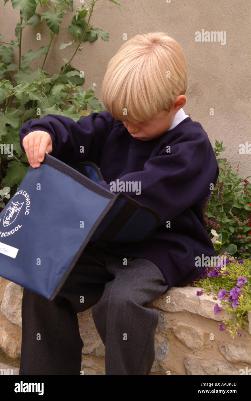 Young boy wearing school uniform looking inside school bag Stock Photo ...