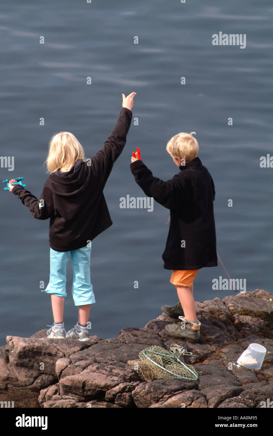Two children standing on a rock and fishing in the sea Stock Photo - Alamy