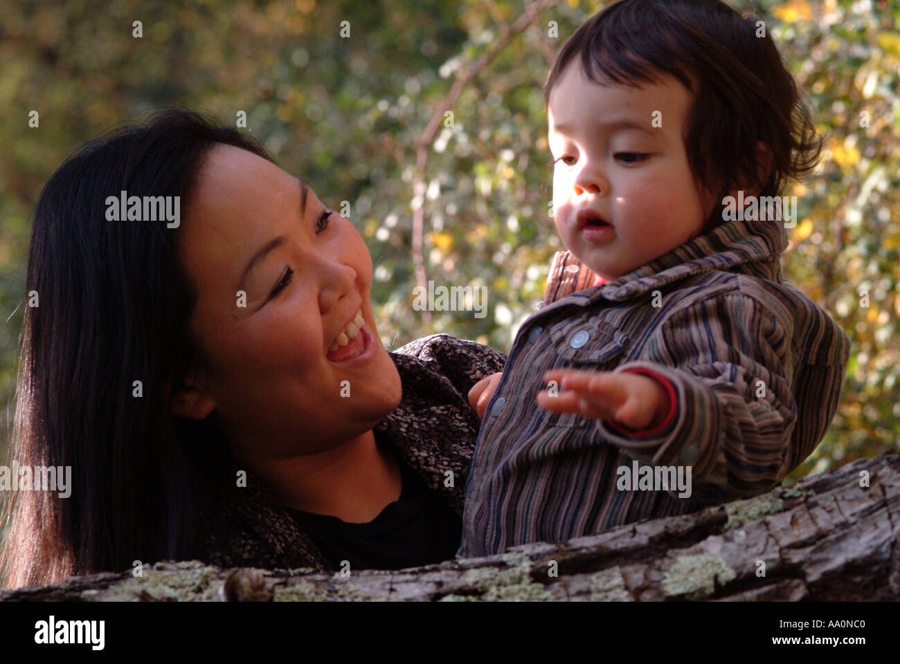 Mother and toddler outside together looking at tree bark and laughing ...