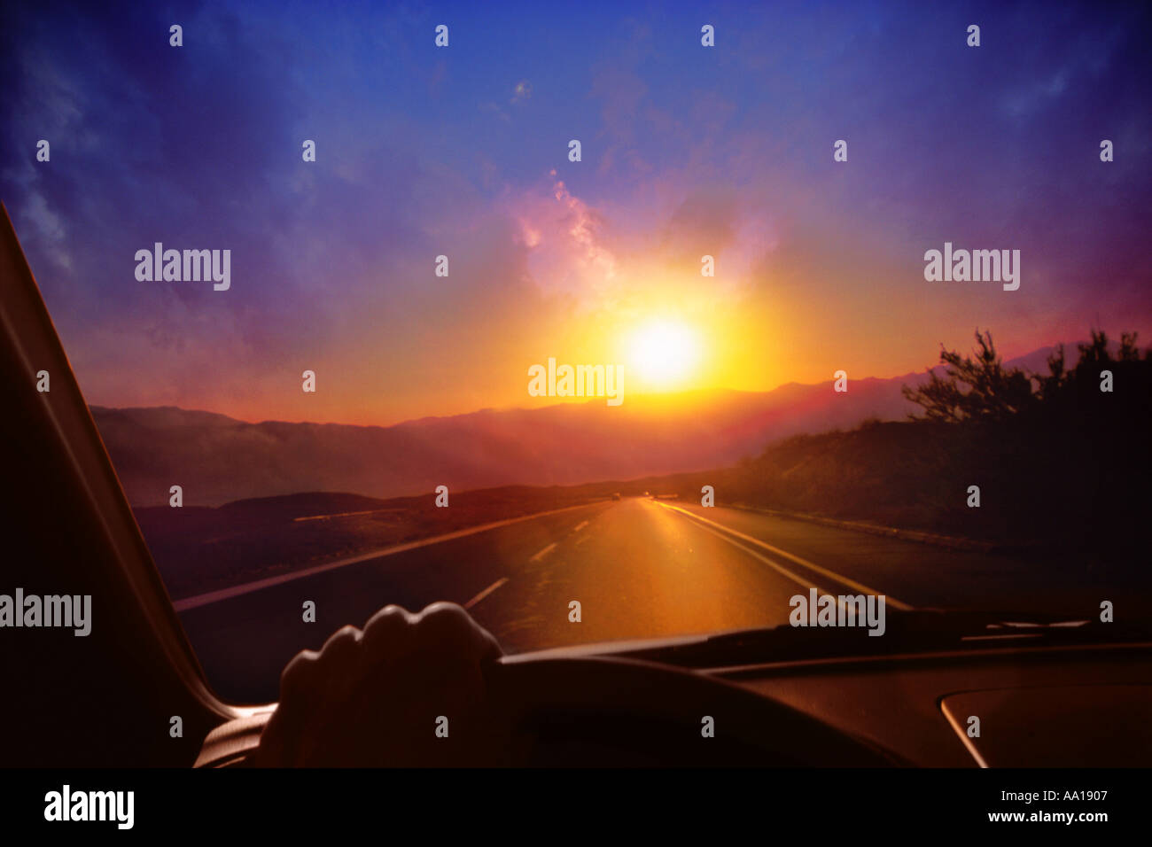 Hand on steering wheel of car on rural road driving into sunset Stock ...