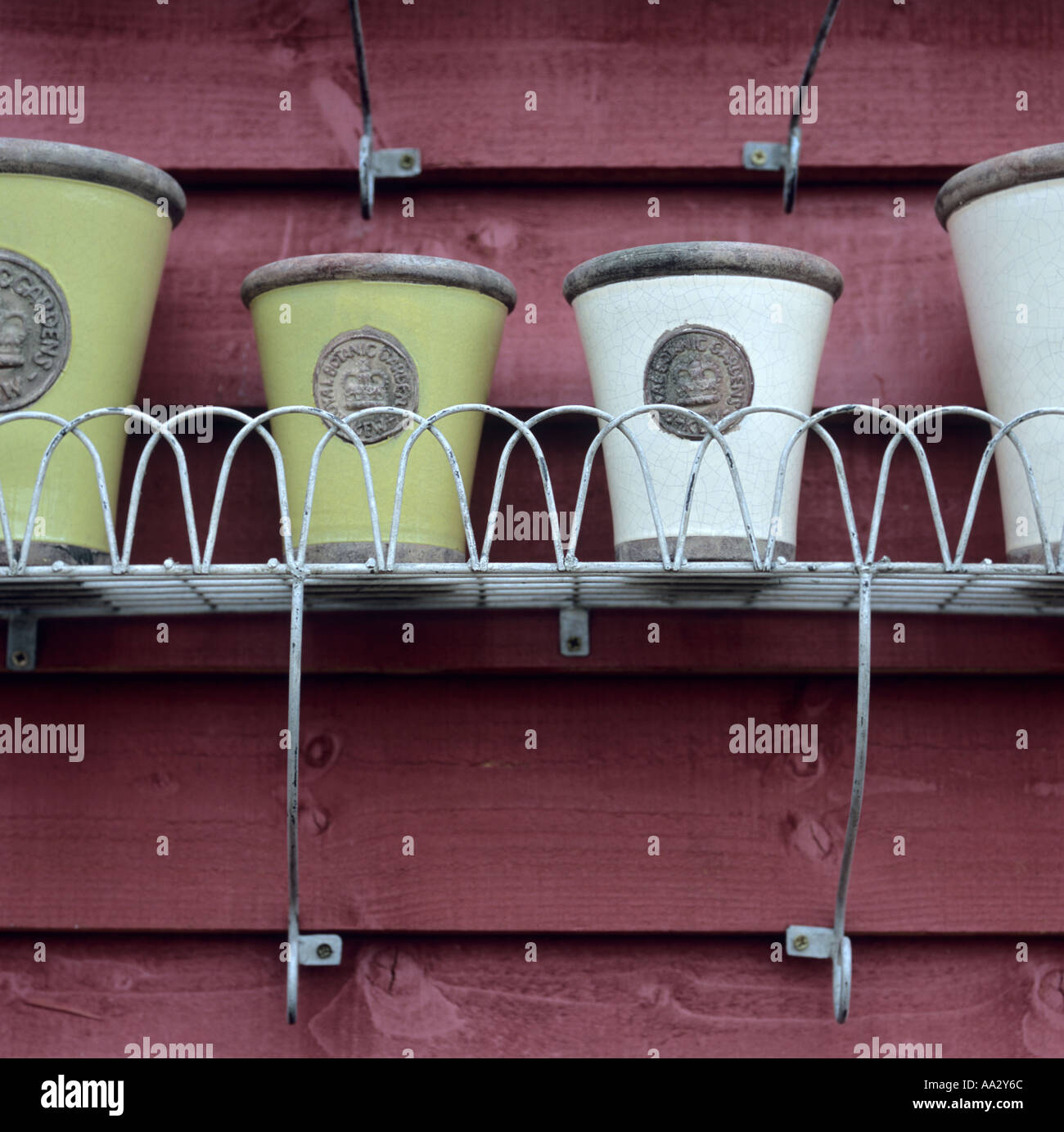 Coloured plant pots on decorative metal shelf against painted shed wall ...