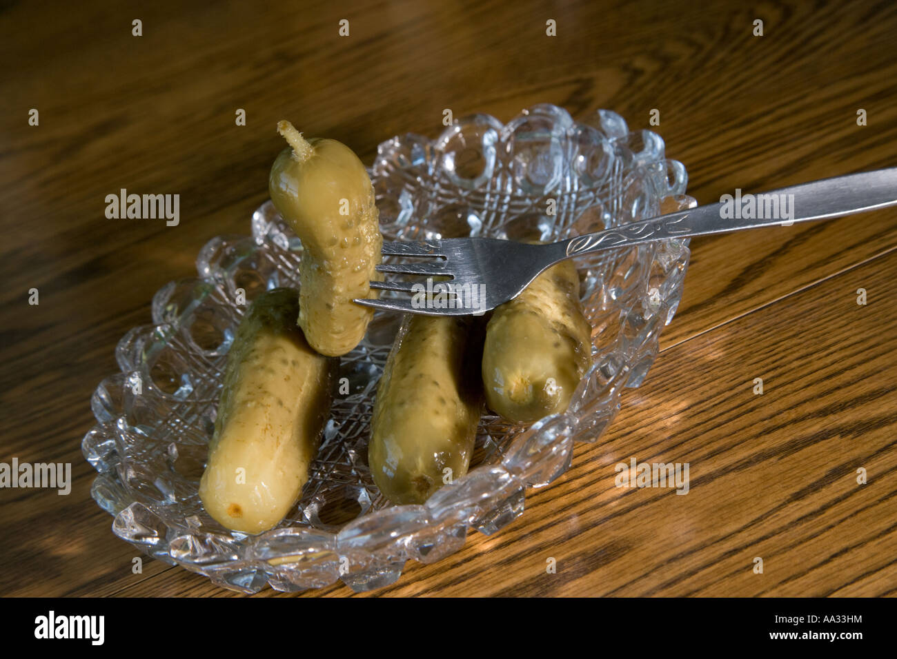 A dill pickle or gherkin on a fork above a glass dish of pickles Stock ...