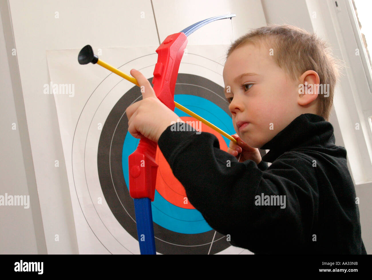 Young boy shooting with toy bow and arrow with bulls eye in background ...