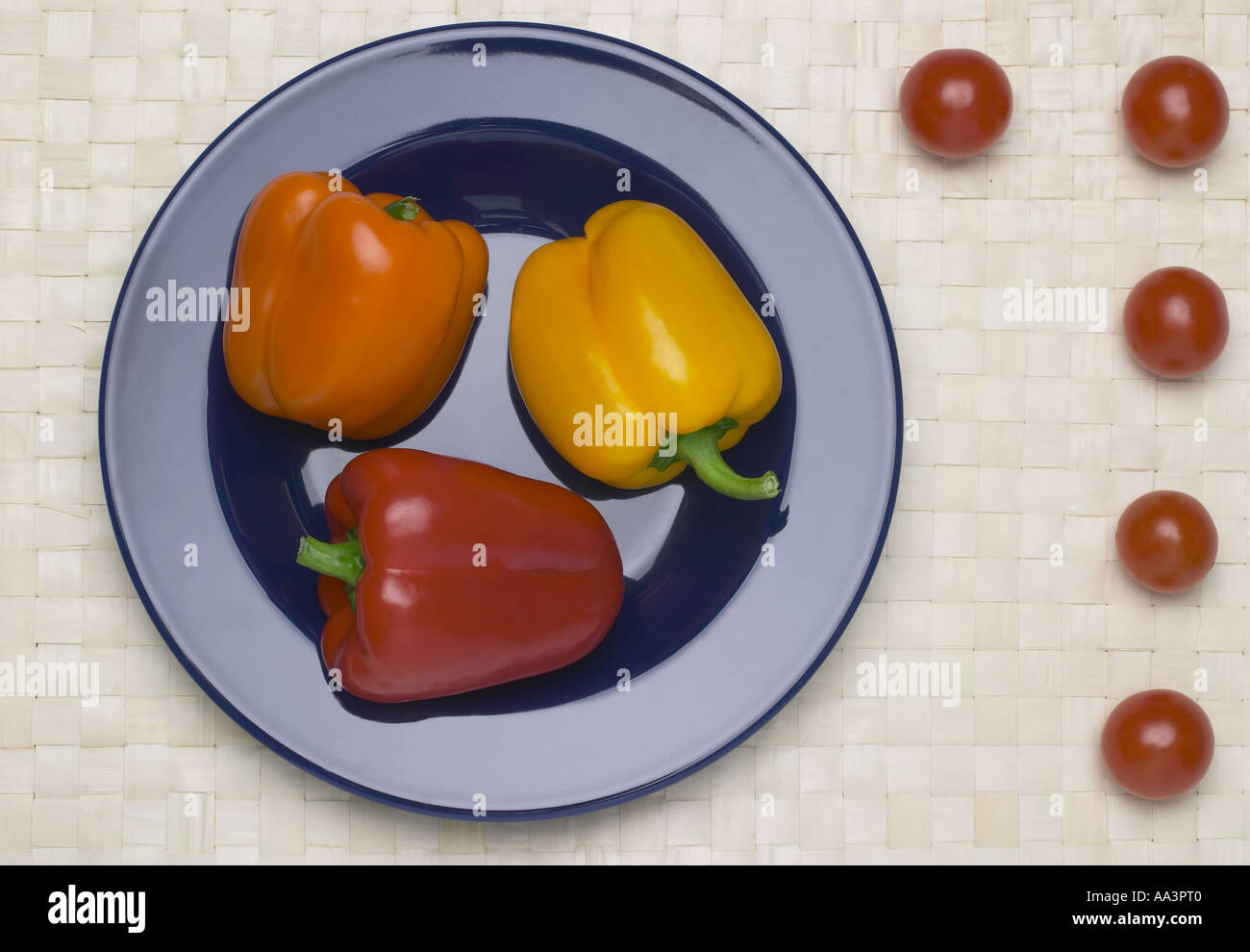 three peppers in the blue plate and little red tomatos all on the light ...
