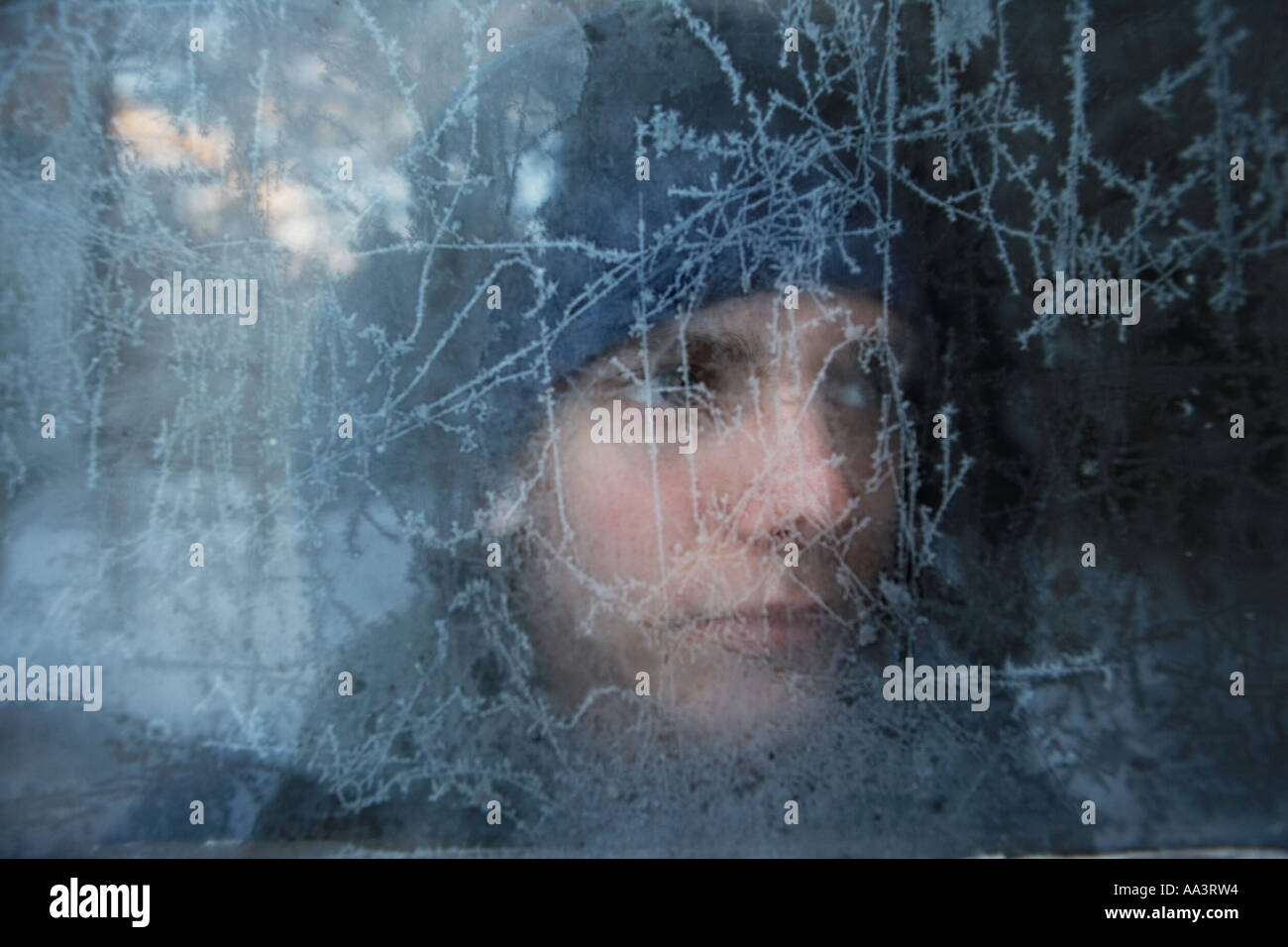 alone young boy looks out through a window with hoar-frost Stock Photo ...