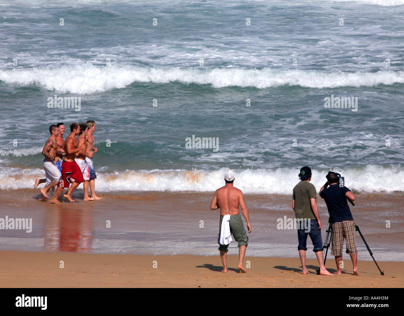 A video production team works with young men running on a beach in ...