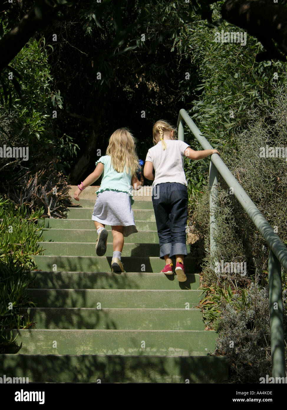 Two blonde little girls walking up a set of green painted steps Stock ...