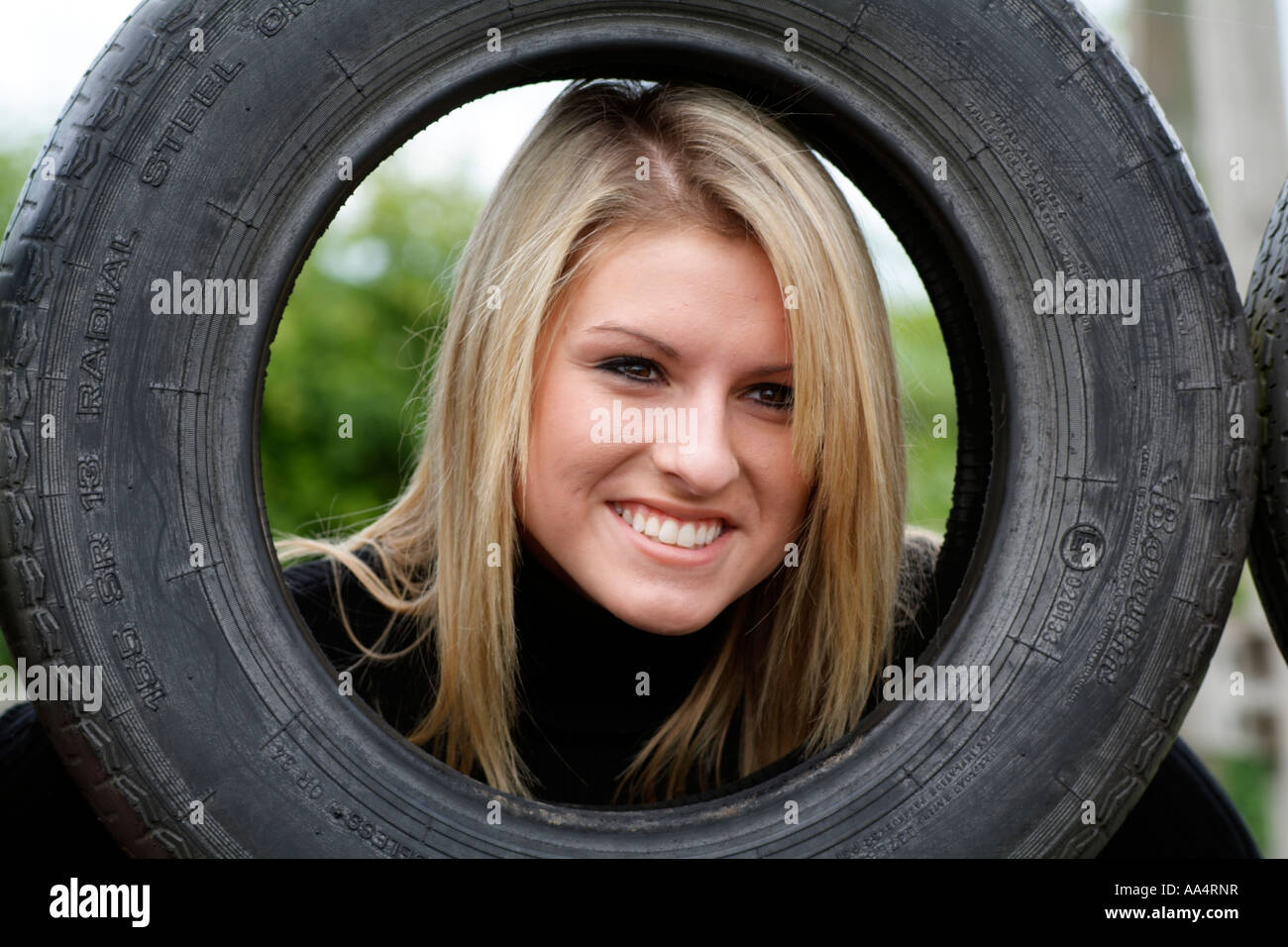 Attractive blonde girl looking through a car tyre Stock Photo - Alamy