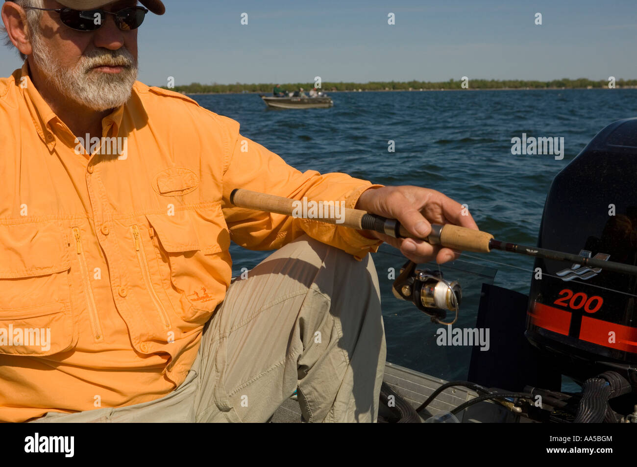 A SMALL FISHING BOAT FLOATS IN THE BACKGROUND OF AN ANGLER FISHING FOR ...