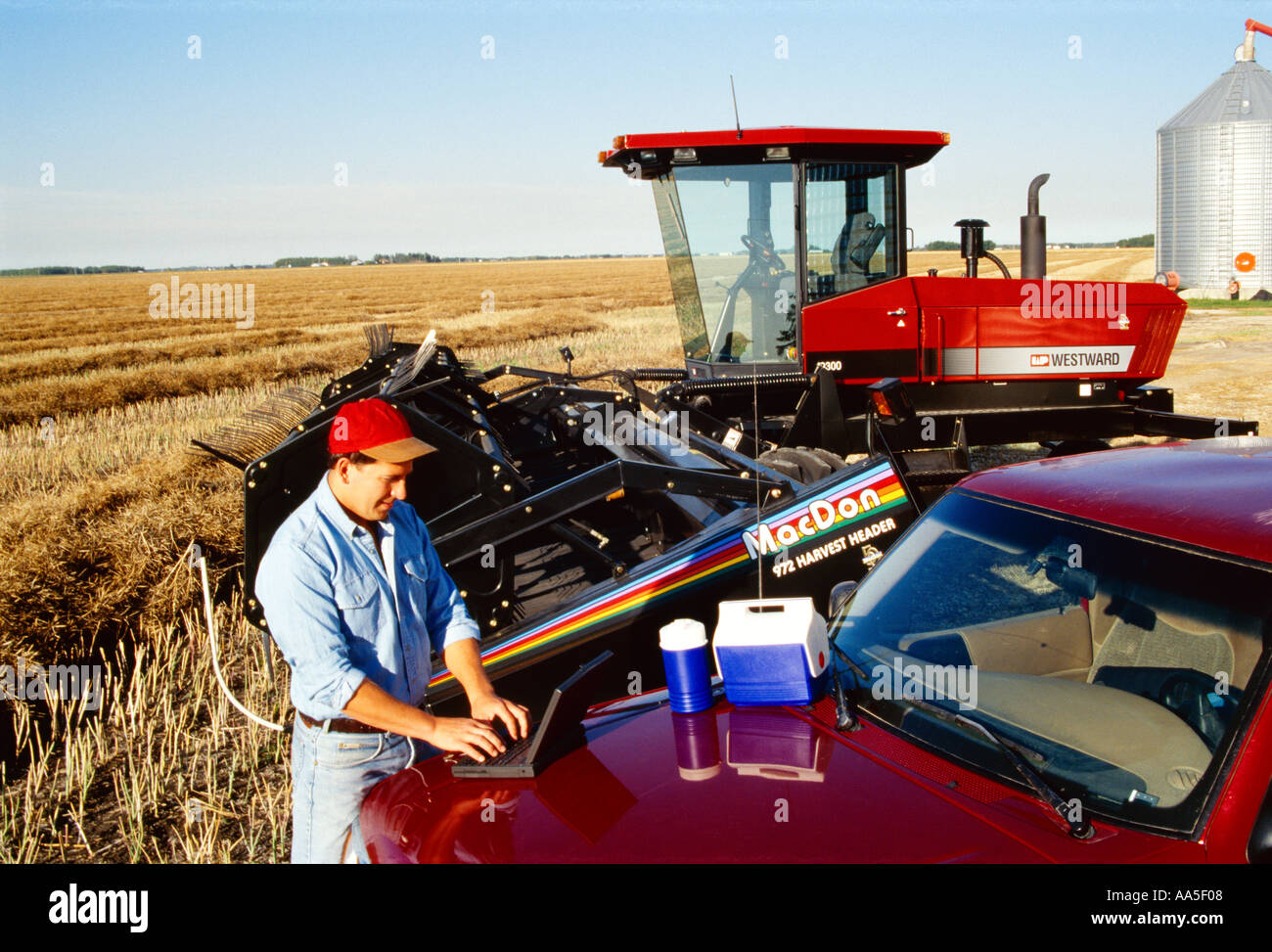 A farmer enters harvesting data into his laptop computer next to a ...