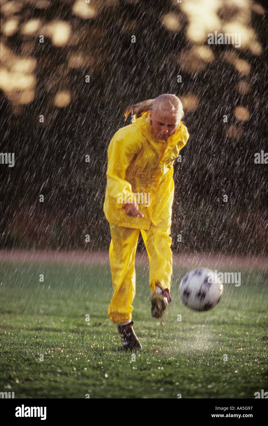 A teenaged girl kicks a football soccerball during a heavy downpour of ...