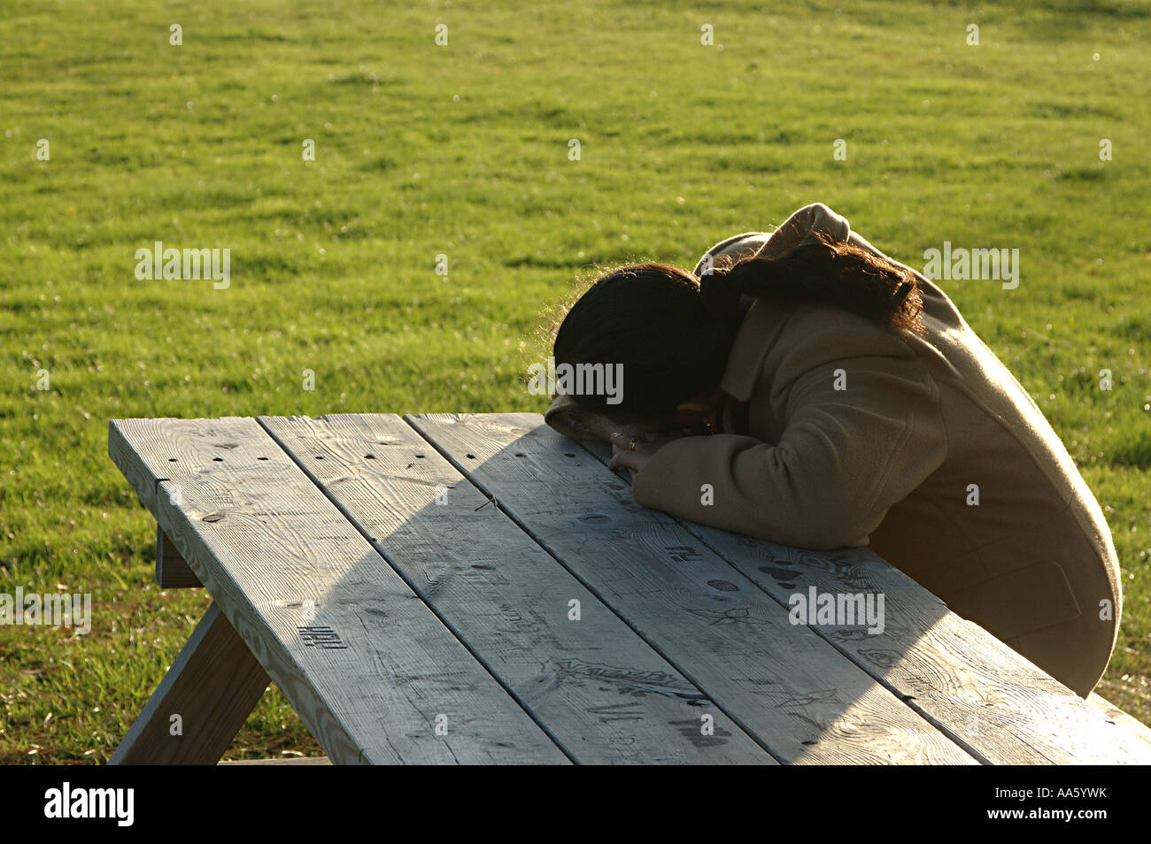 Indian senior woman, sitting on bench and resting her head on table ...