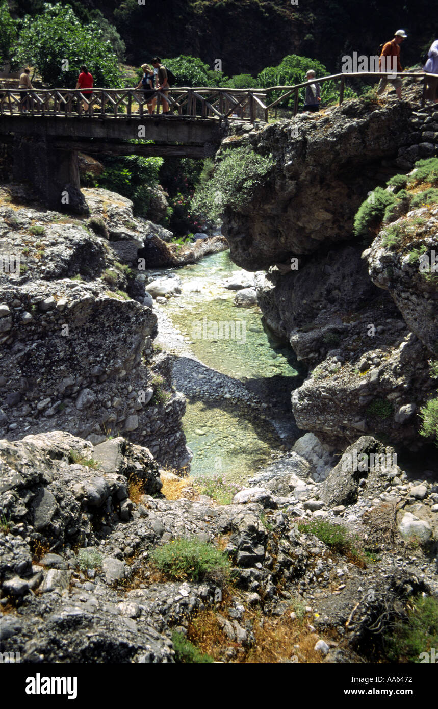 Hikers crossing the sunlit wooden bridge over the river and rocky ...
