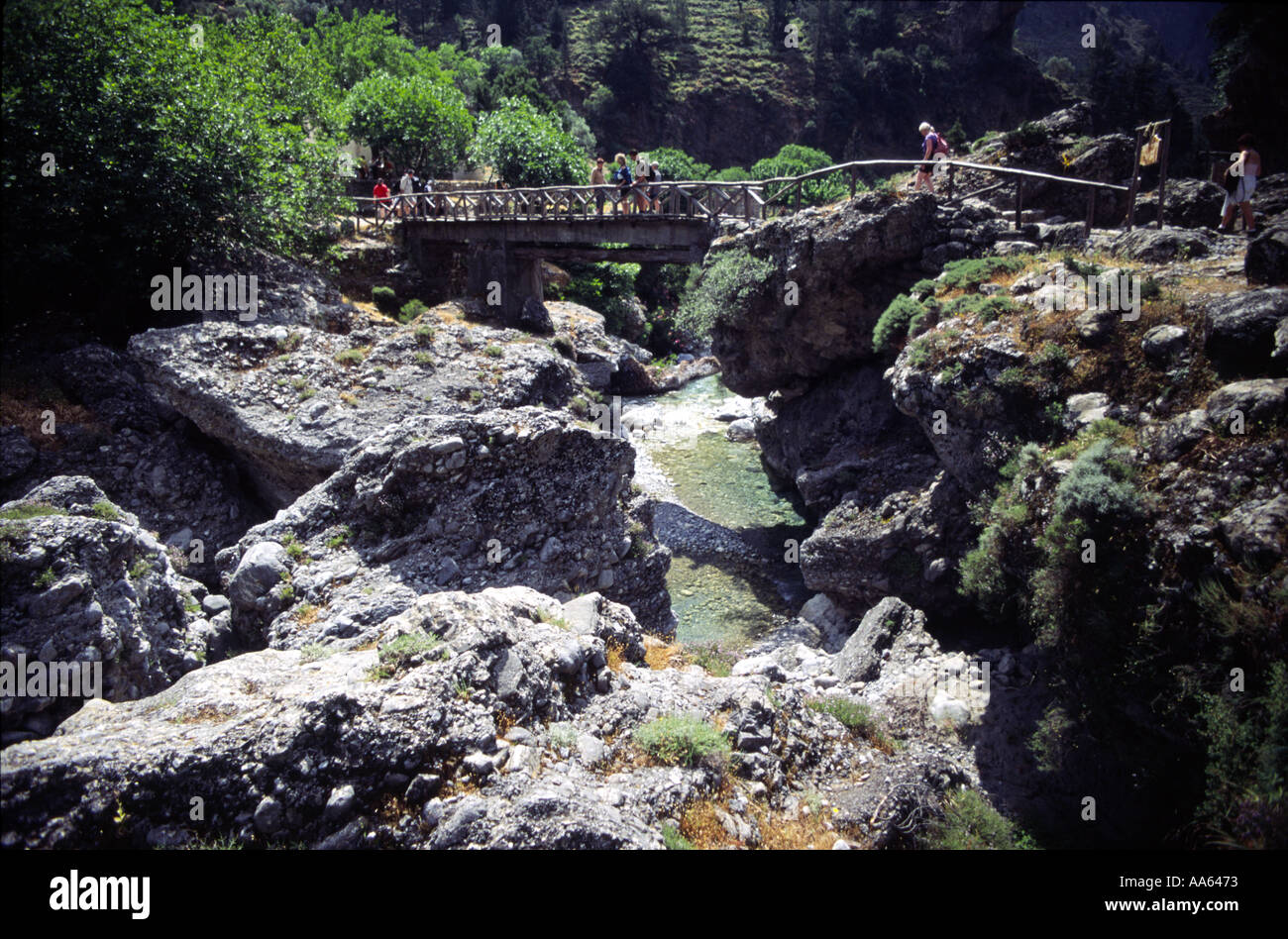 Hikers crossing the sunlit wooden bridge over the river and rocky ...