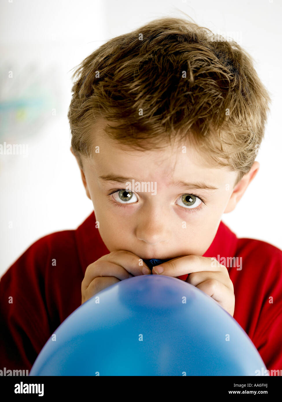 boy 7 blowing up a blue balloon for a birthday party and looking timid ...