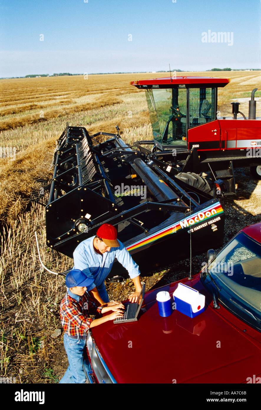 A farmer with his son enters harvesting data into a laptop computer ...