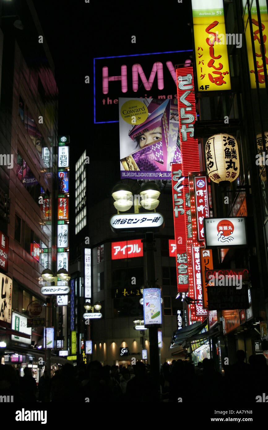 people crowd underneath neon signs in the Shibuya district of Tokyo ...