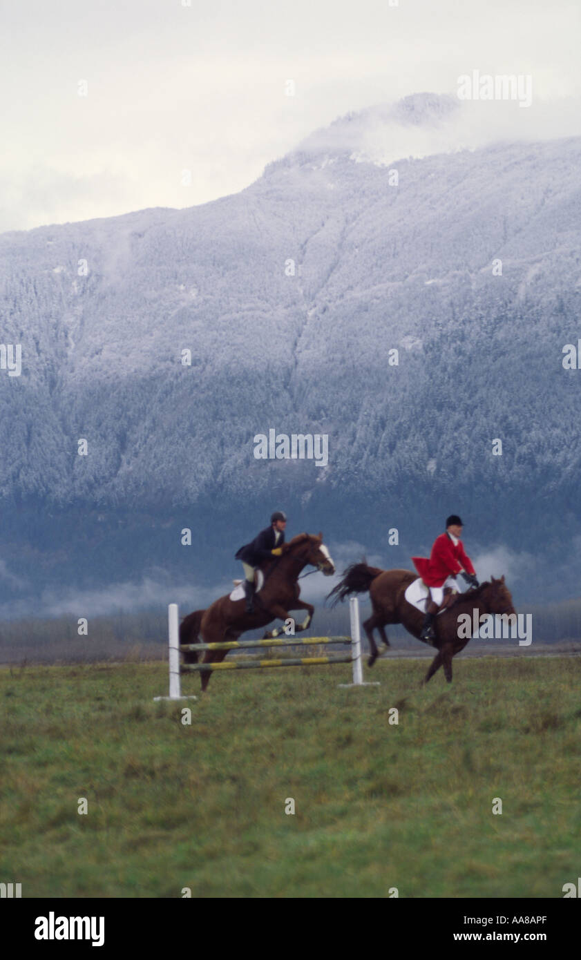 Two English Fox hunt riders jump hurdle with snowy mountains in ...