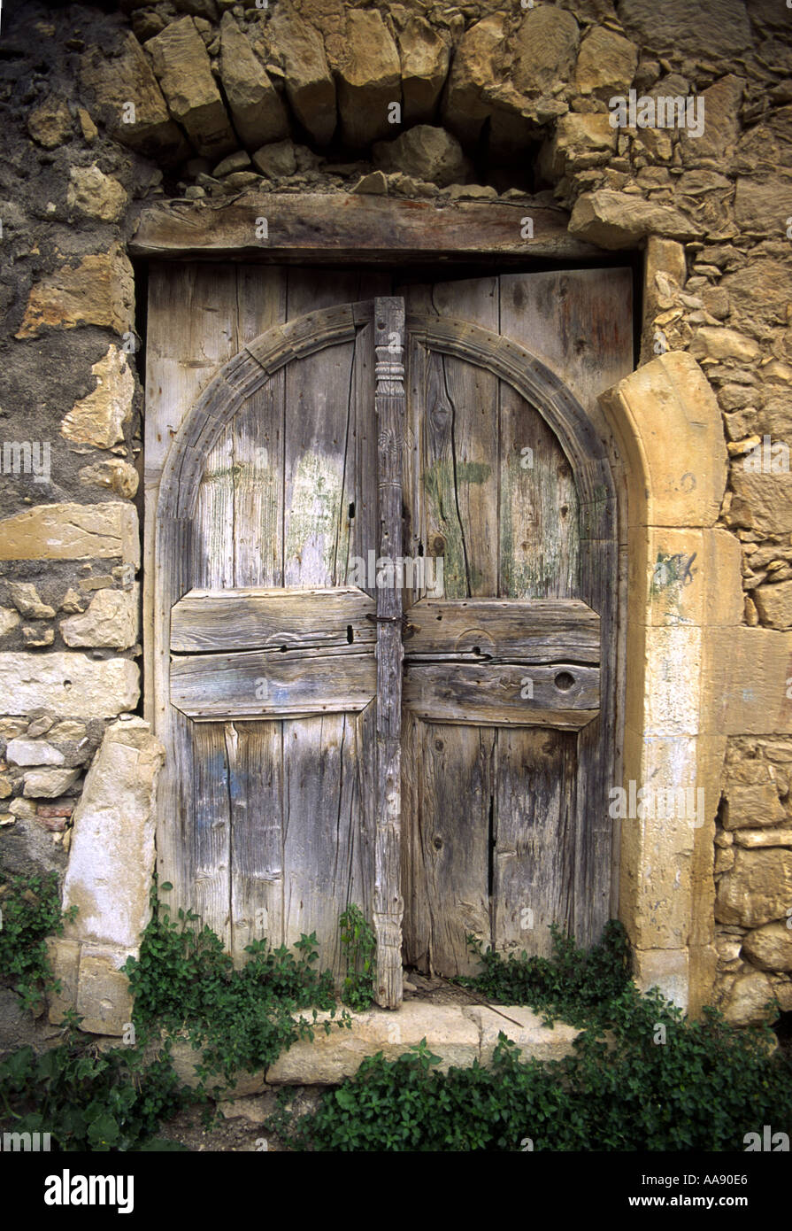 Plain wooden unpainted semi arched door in a crumbling limestone wall ...