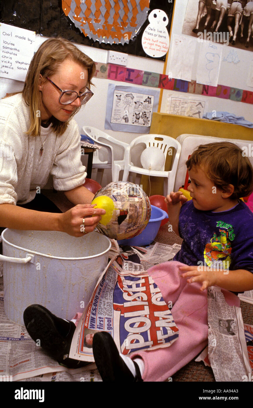 Young adult carer helping young children make paper mache objects ...