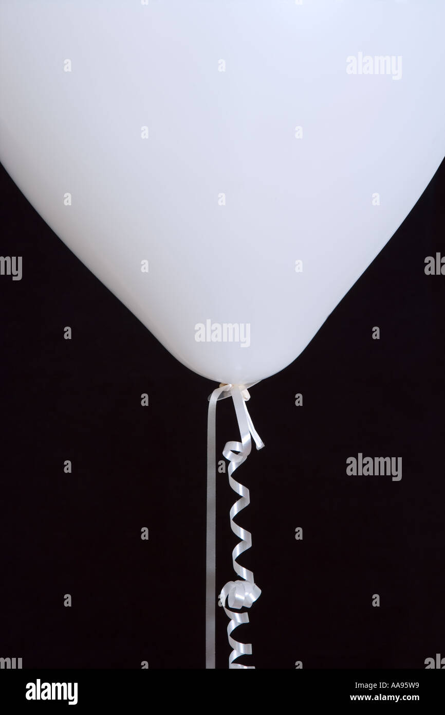 White balloon and curled ribbon against black background, close-up ...