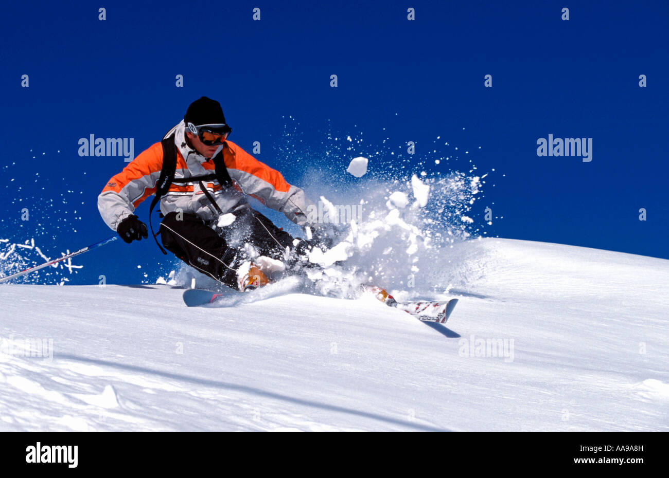 Extreme male skier coming very fast over the brow of a hill kicking up ...