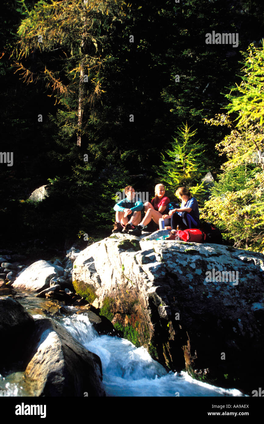 Group of walkers taking a rest break on a boulder beside a river in ...