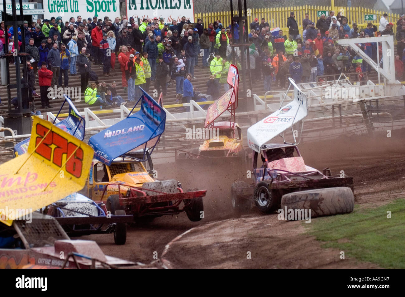 stock cars racing around a dirt circuit being watched by a standing ...