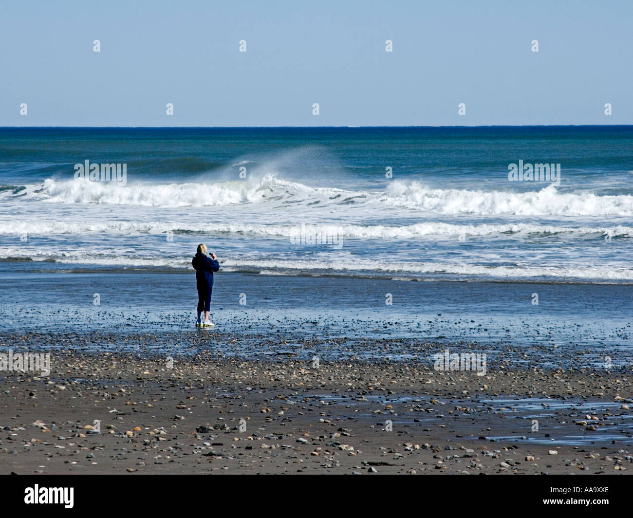 A woman stands on an empty beach looking out towards the ocean Stock ...
