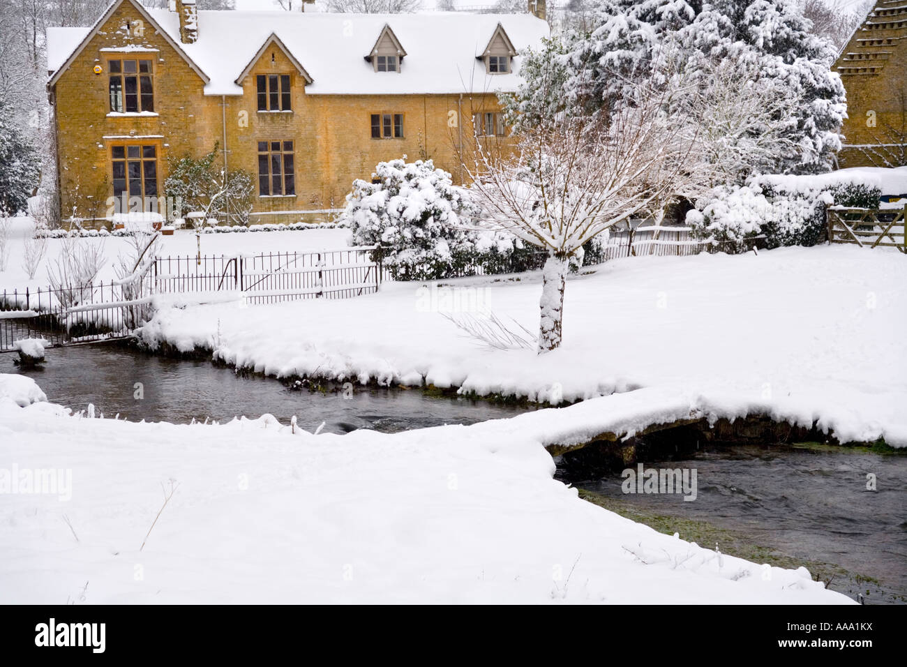 Winter snow on an old farmhouse beside the River Eye in the Cotswold ...