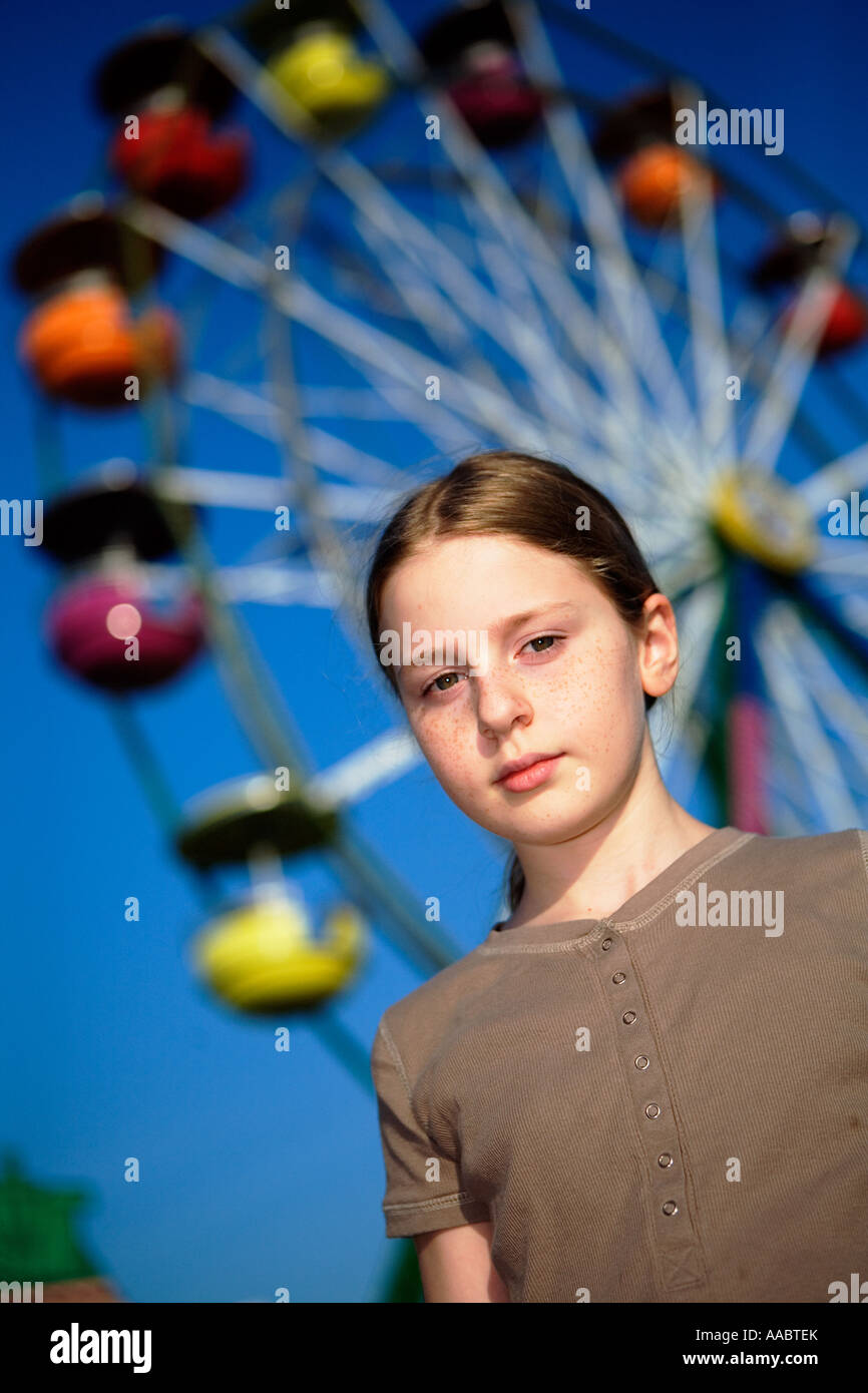 girl standing in front of ferris wheel at carnival or fair looking ...