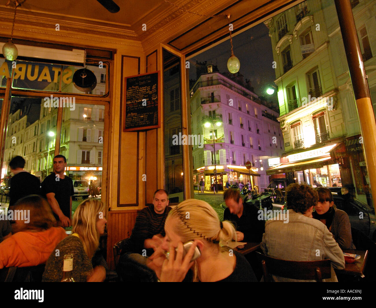 Interior of a busy cafe le Progres with Montmartre at night seen ...