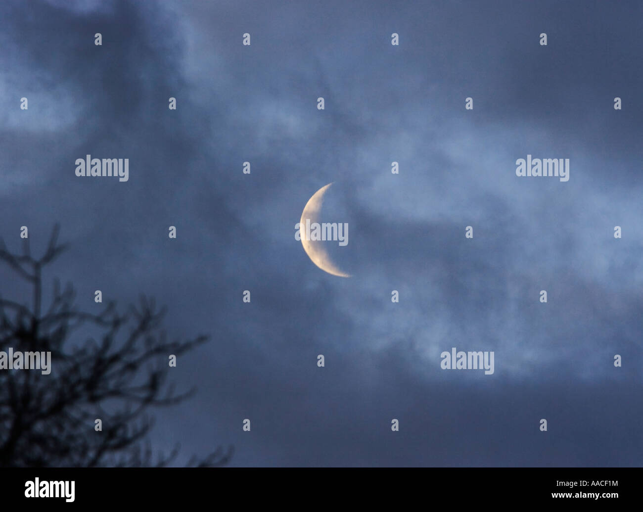 Dramatic bright glow of crescent moon against swirling grey clouds ...