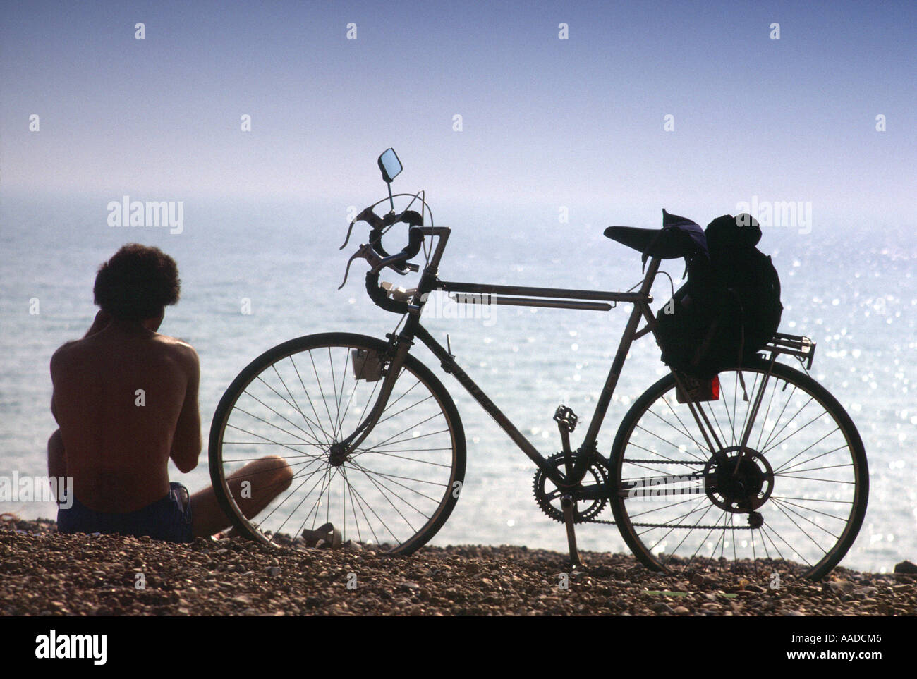 Man sitting sunbathing on pebble beach with racing bycycle England UK ...