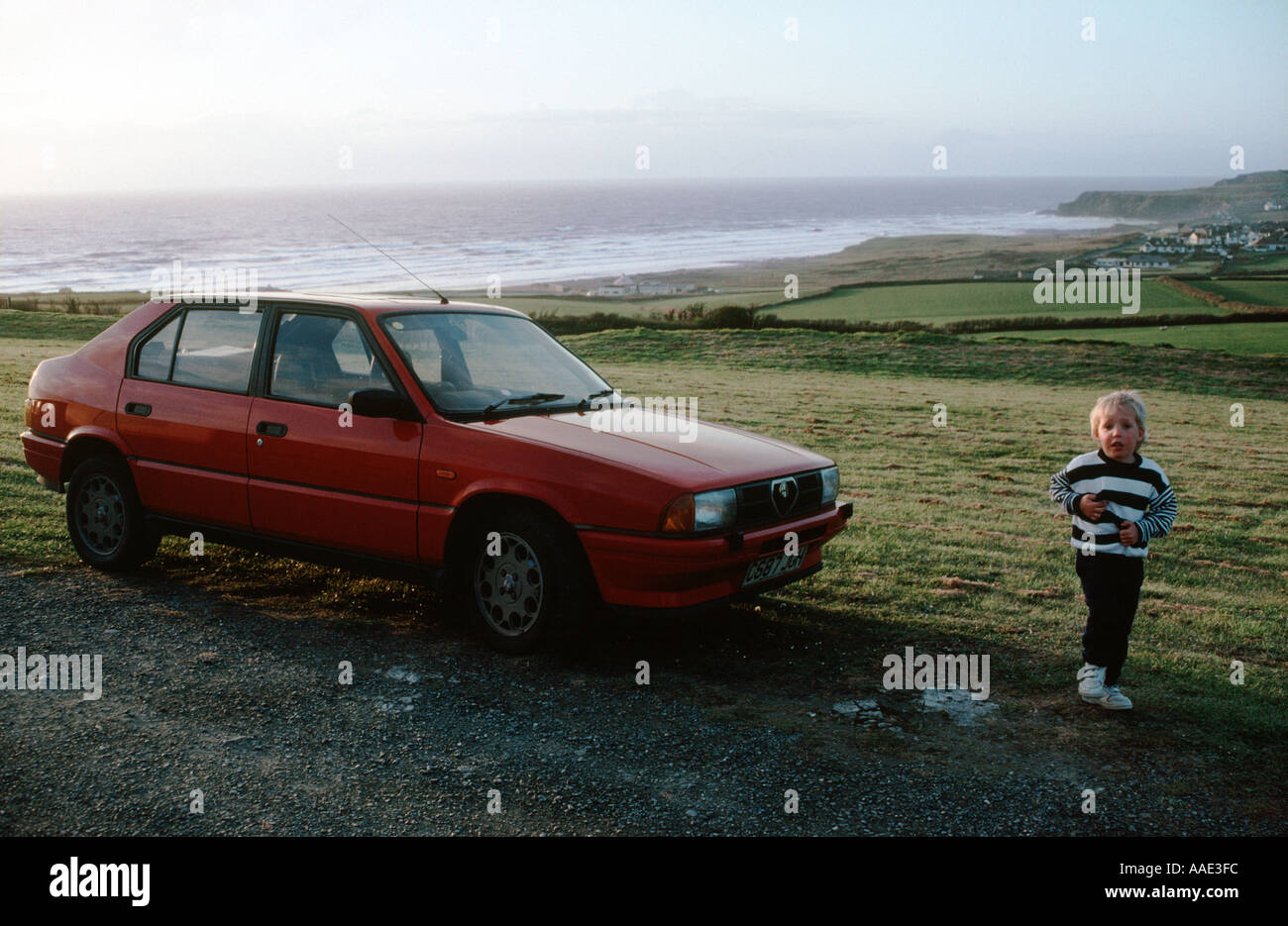 Red Alfa Romeo 33 parked on a hill overlooking the sea in evening light ...