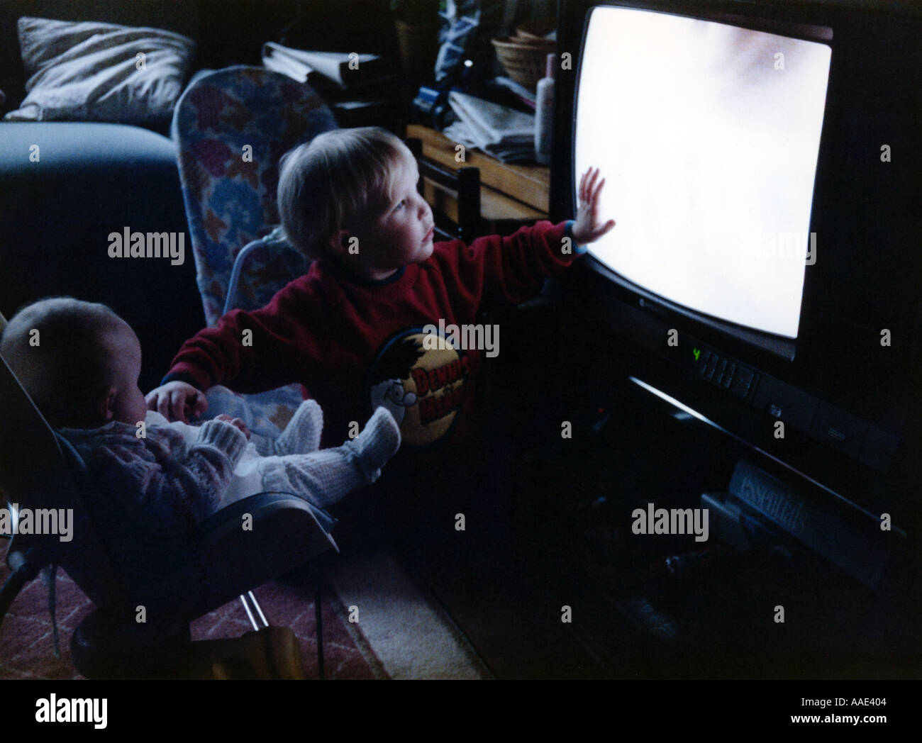 Small boy and baby sister watching television the boy gesturing as if ...