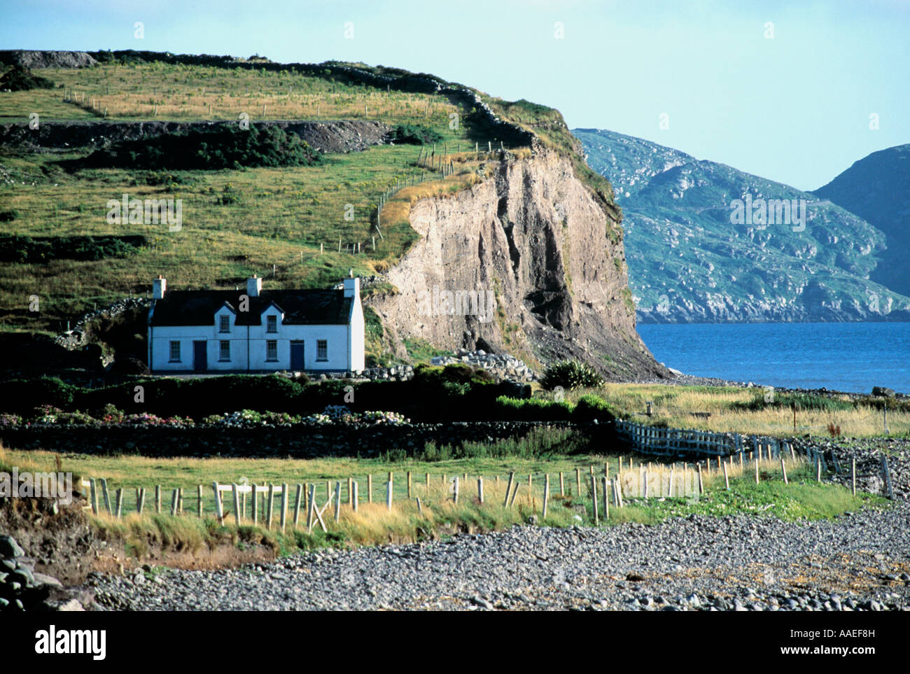 small irish cottage on a raised beach under a high sea cliff, county ...