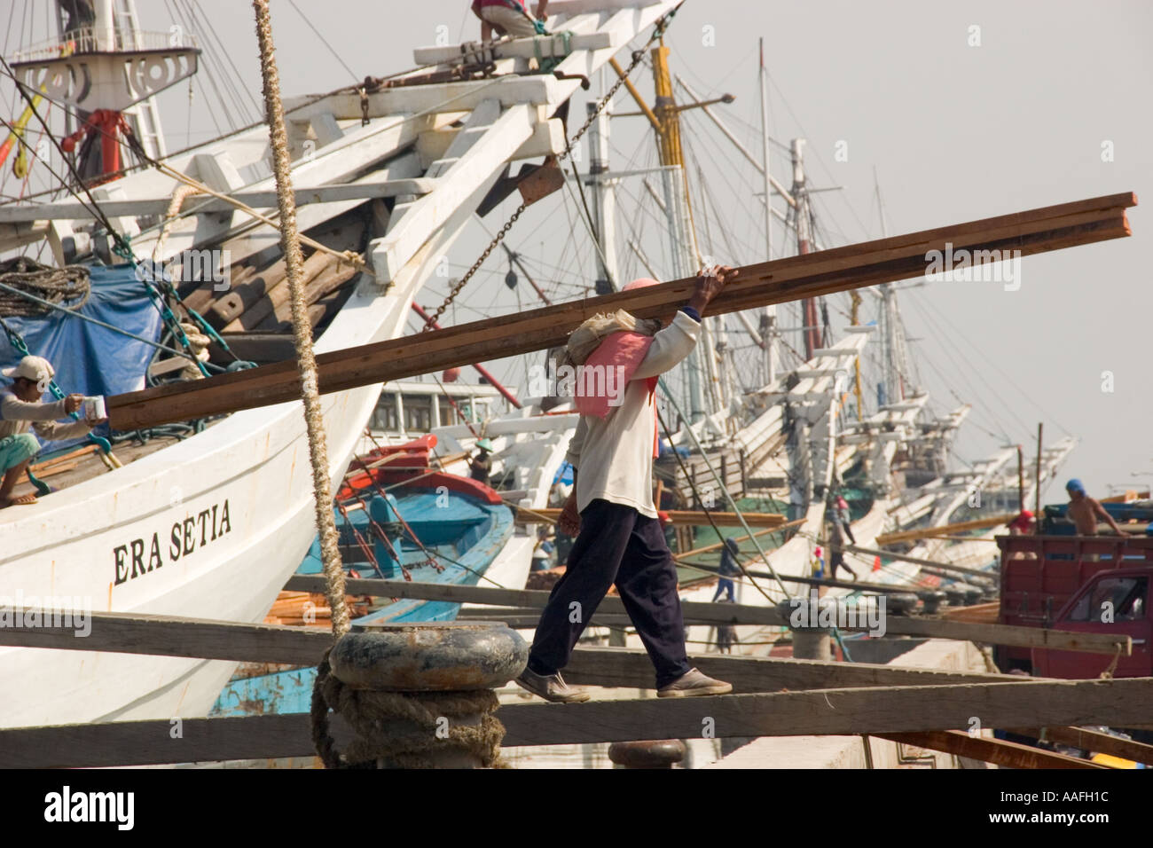 Man unloading timber from a wooden sailing ships or prahu from Sulawesi ...
