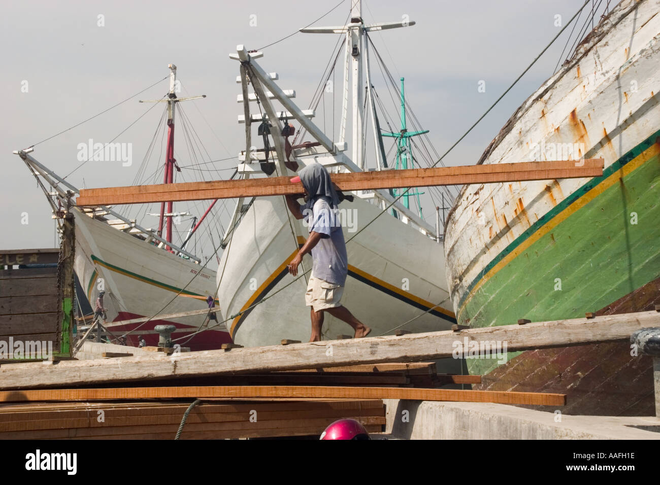 Man unloading timber from a wooden sailing ship or prahu from Sulawesi ...