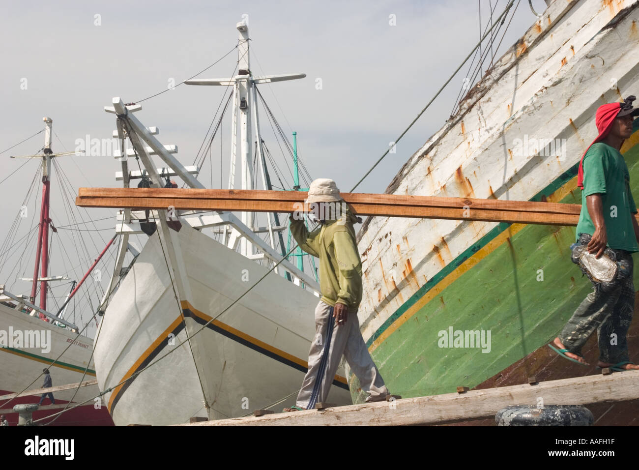 Man unloading timber from an old style wooden sailing ship or prahu ...