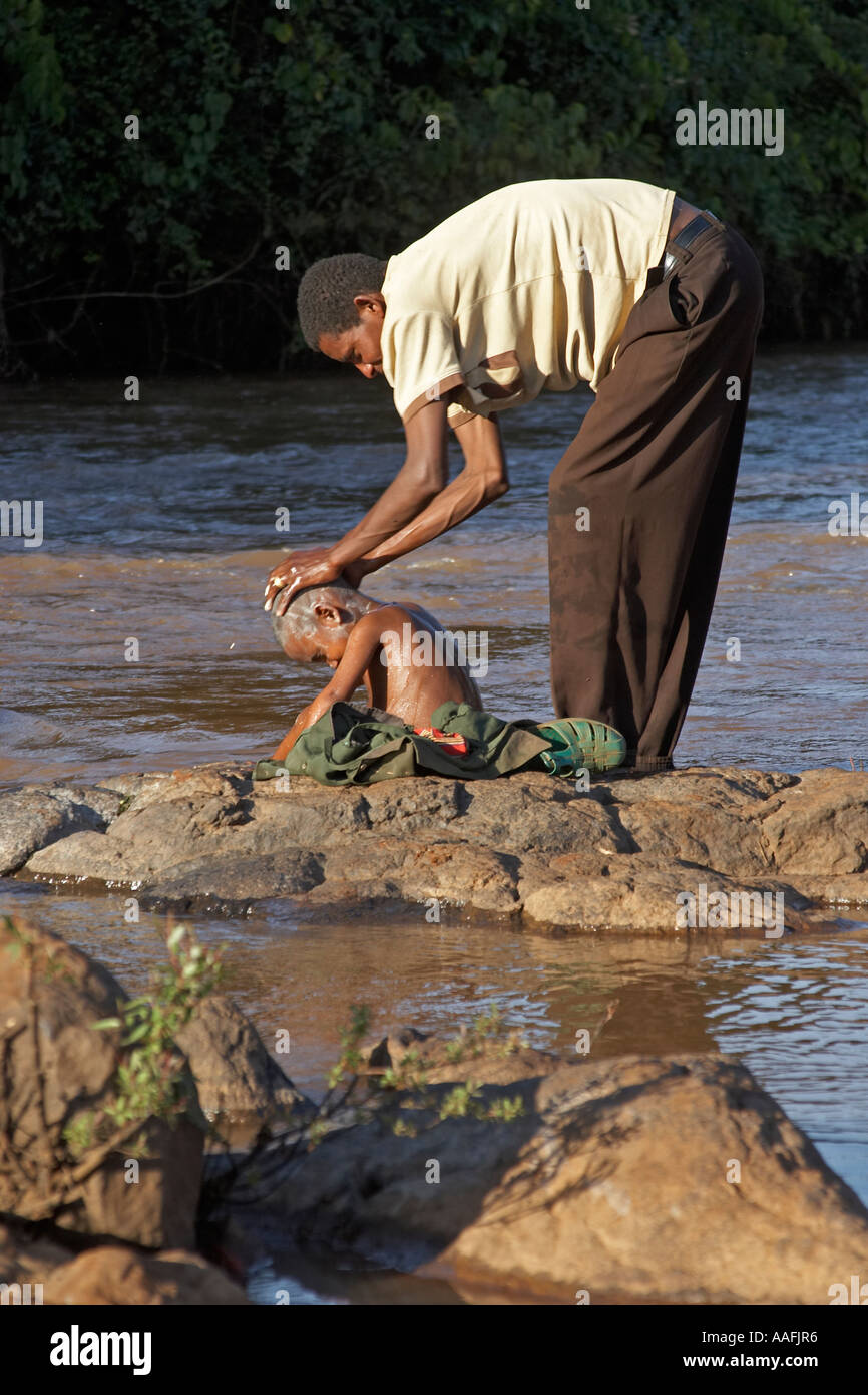 Local man father washing his son boy child with soap in the river near ...