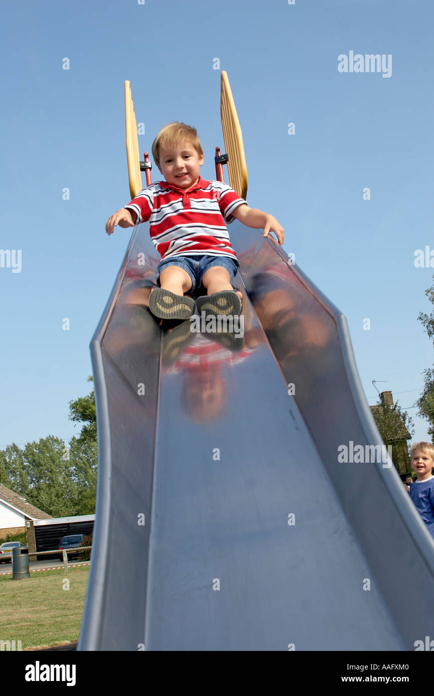 Youg boy child playing sliding down a metal slide outdoors with blue ...