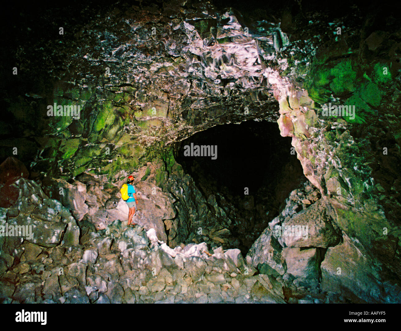 Female caver in the entrance to Pictograph Cave lava tube with algae ...