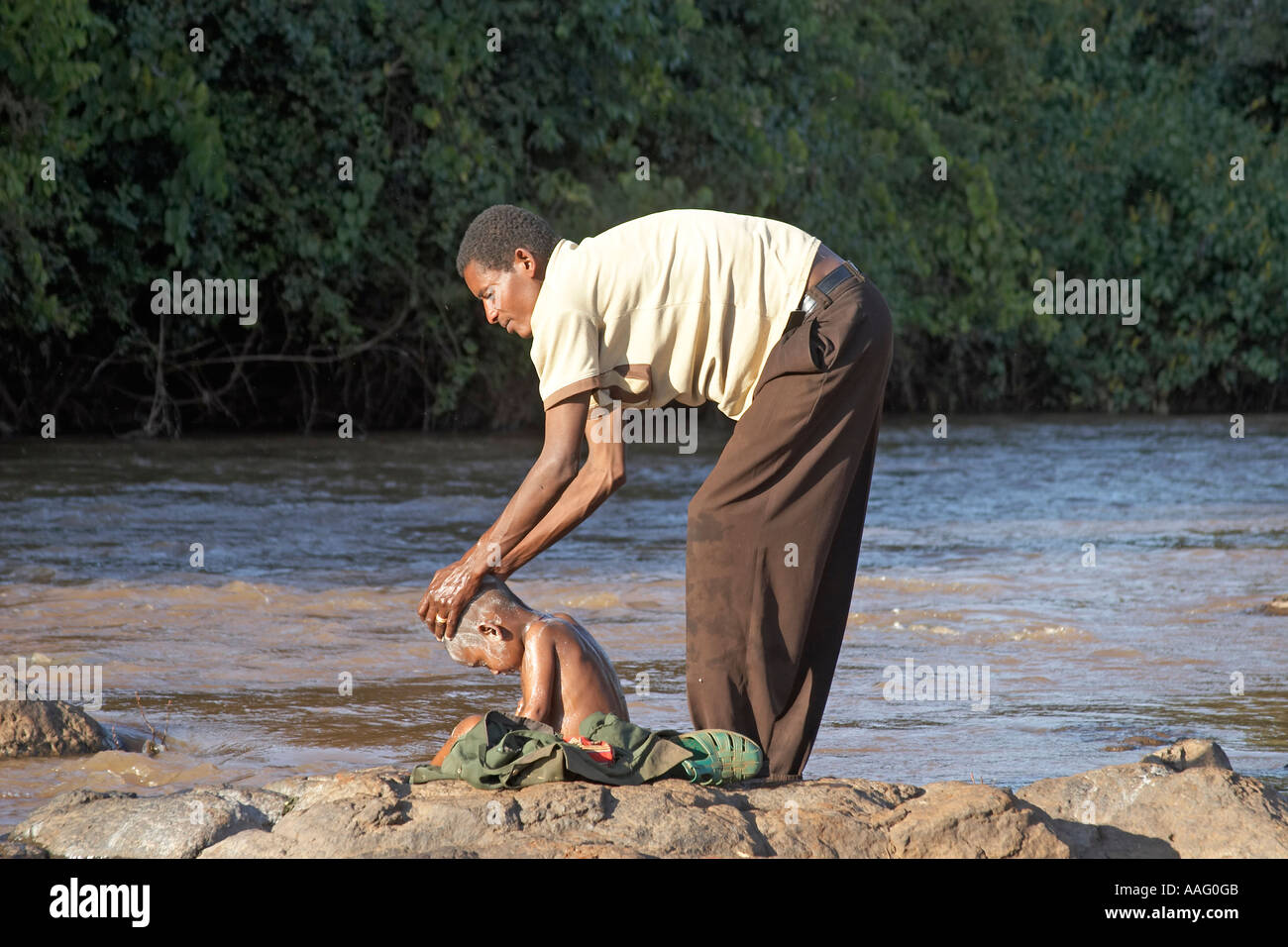 Local man father washing his son boy child with soap in the river near ...